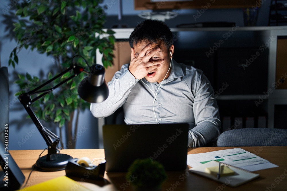 Young chinese man working using computer laptop at night peeking in ...