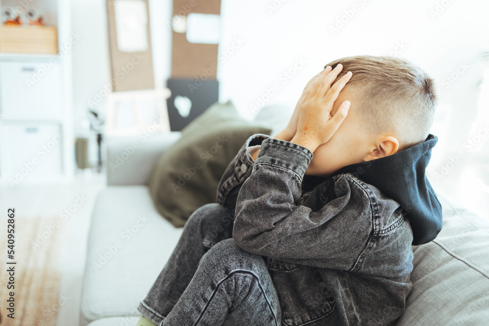 Little boy suffering from child abuse curled up on the sofa. Depressed ...