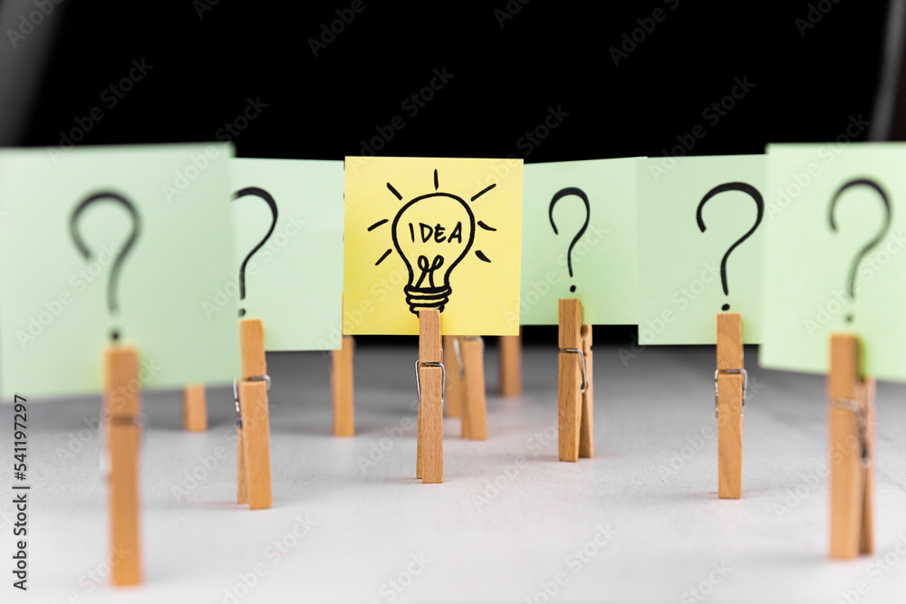 Light bulb doodle drawn on sticky note among many question marks. Hand drawn doodle lineart ...