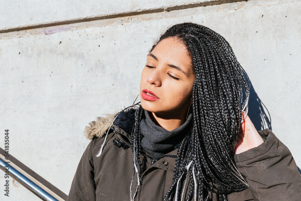 Tranquil female with braids touching black hair and enjoying sunny ...