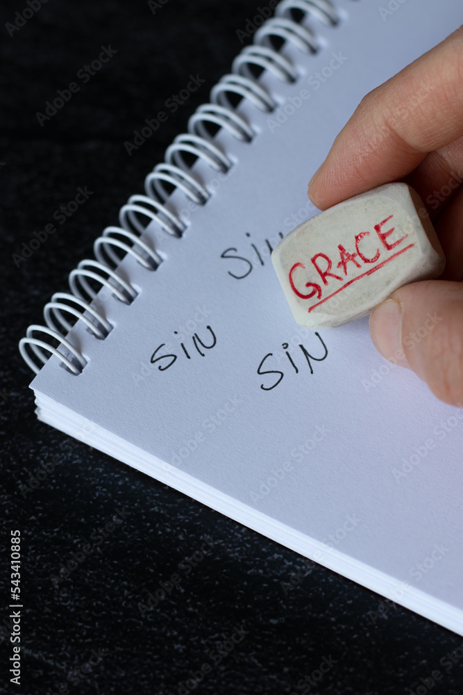 Word "grace" written on eraser in human hand placed over notebook page ...