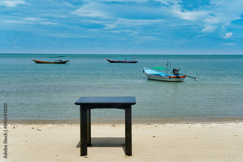 Table on the beach with longtail boats in the background. Teams/zoom ...