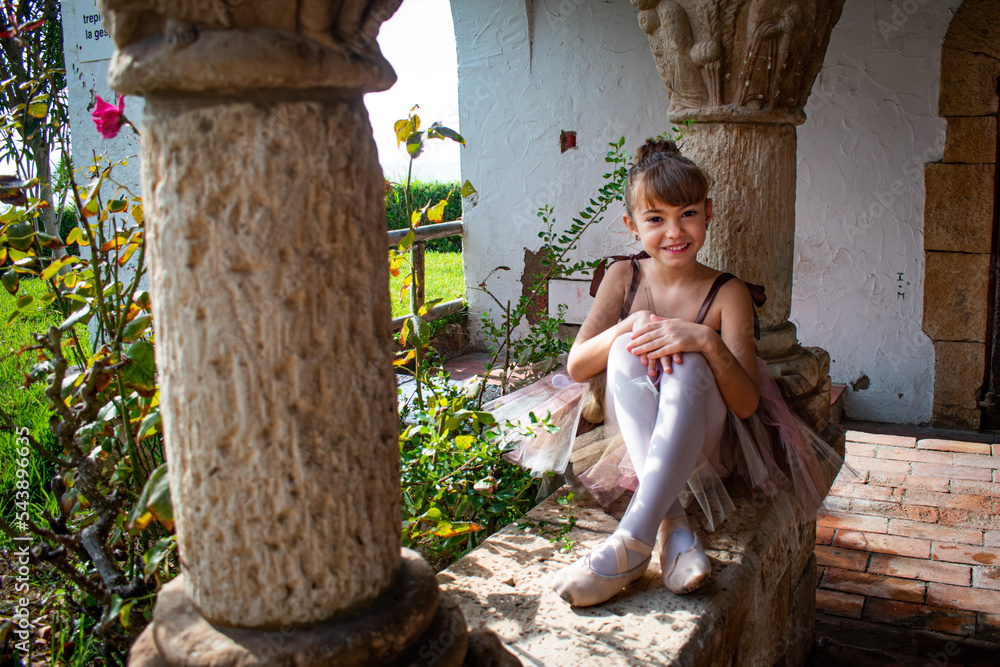 Niña pequeña bailando ballet en un jardín con muros románicos de piedra ...
