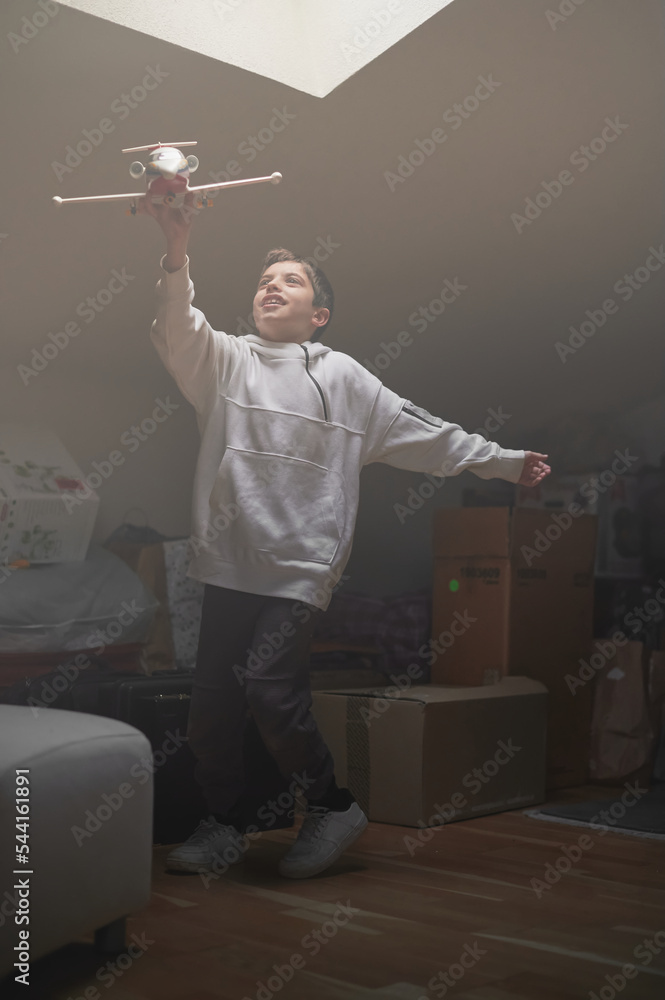 Preteen boy playing with a toy airplane pretending to fly in the attic ...