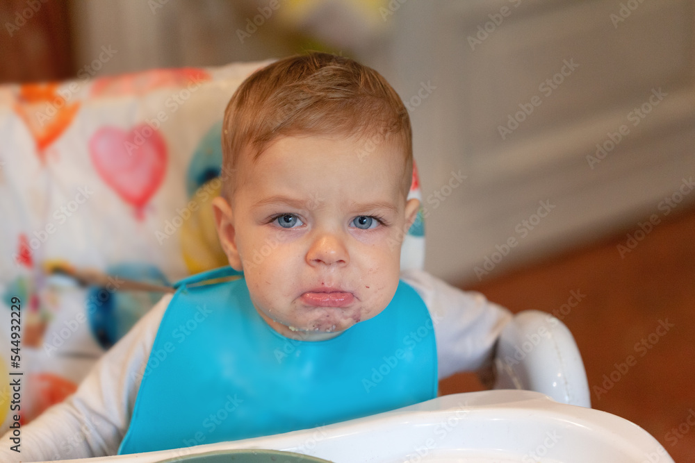 Caucasian Baby eleven months old wearing a bip sits in a highchair ...