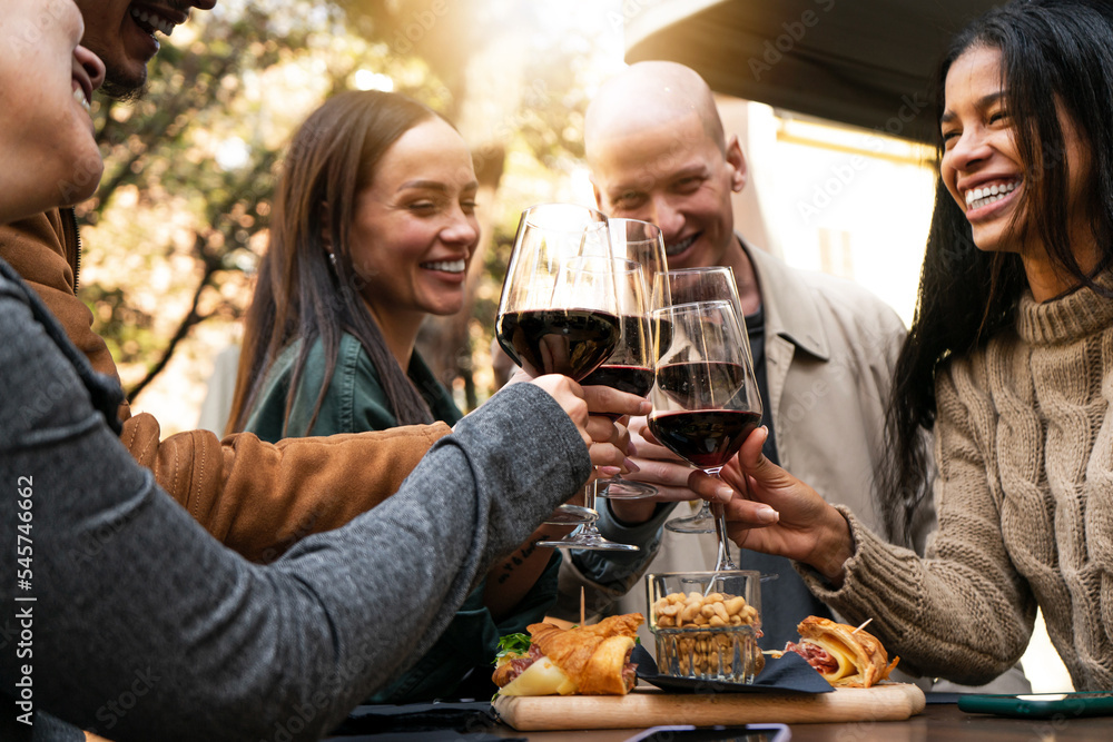 Young smiling friends toasting red wine at restaurant pub at happy hour ...