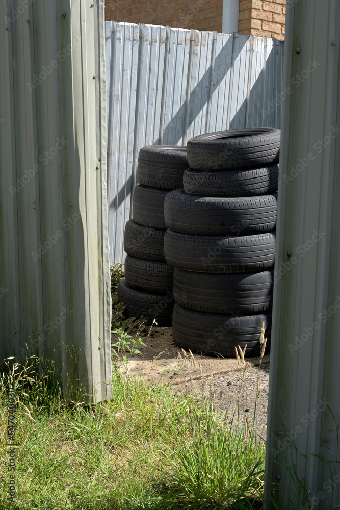 Used car tires piled up against a metal fence awaiting recycling ...
