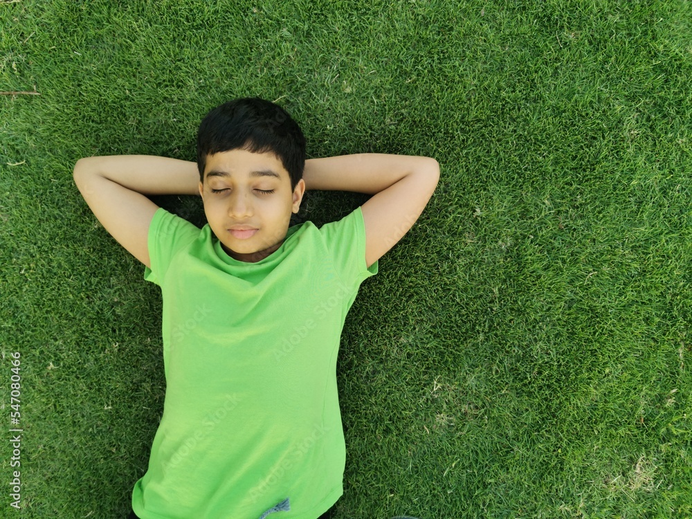 Child boy lie down on grasses or lawn under warm sunlight. Kid closed his eyes and flew away ...
