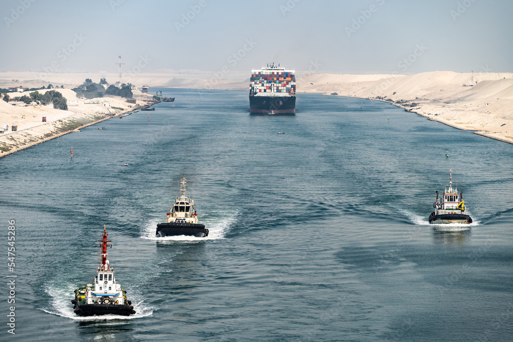 Huge cargo ships with pilot boats navigate by Suez Canal, Egypt. Concept of transportation and ...