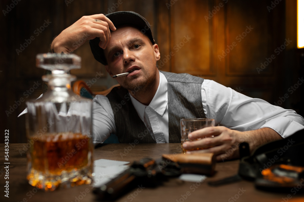 Tipsy man smoking at table with cards and pistol in vintage casino ...
