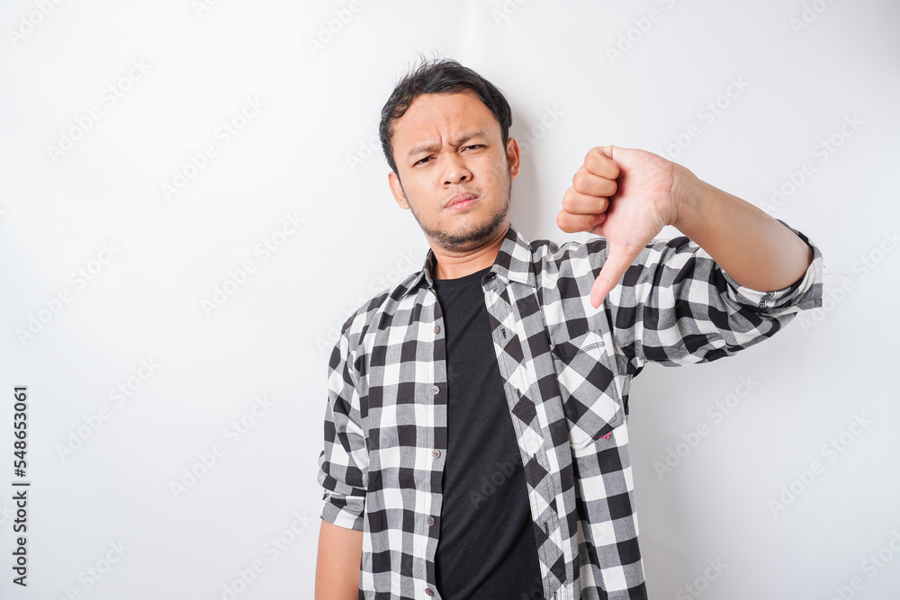 Disappointed Asian man wearing tartan short gives thumbs down hand ...
