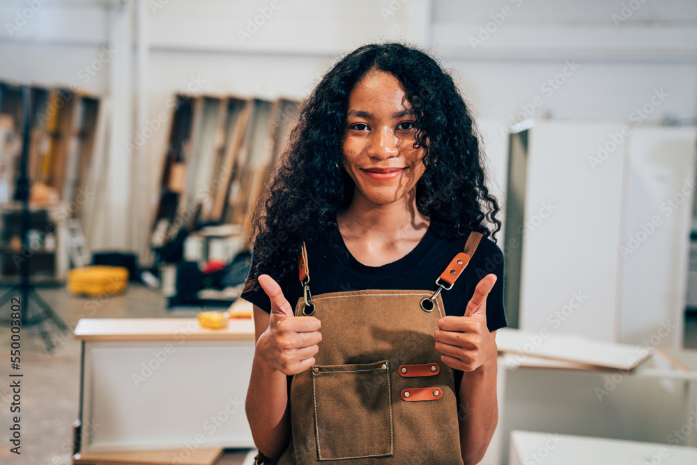 Portrait of female carpenter doing some work in a woodshop and smiling ...