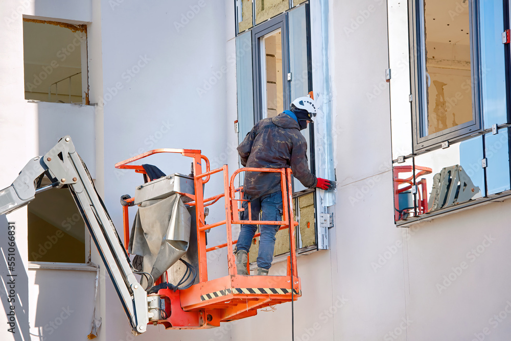 Man in lift bucket caulk, seal exterior window with putty knife ...