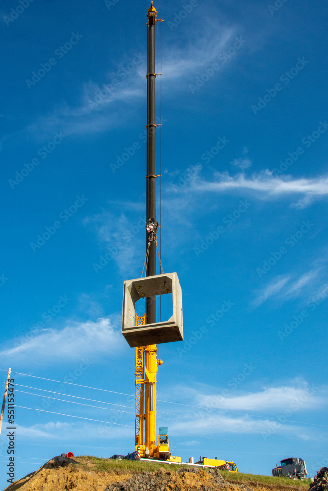 Hydraulic crane lifting a section of rectangular concrete culvert above ...