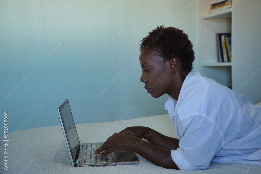 African American woman in a white shirt and lying in bed, working with ...