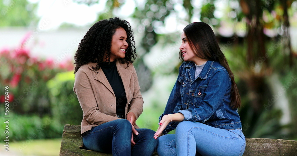 Two diverse girls talking outside together, real life laugh. Female ...