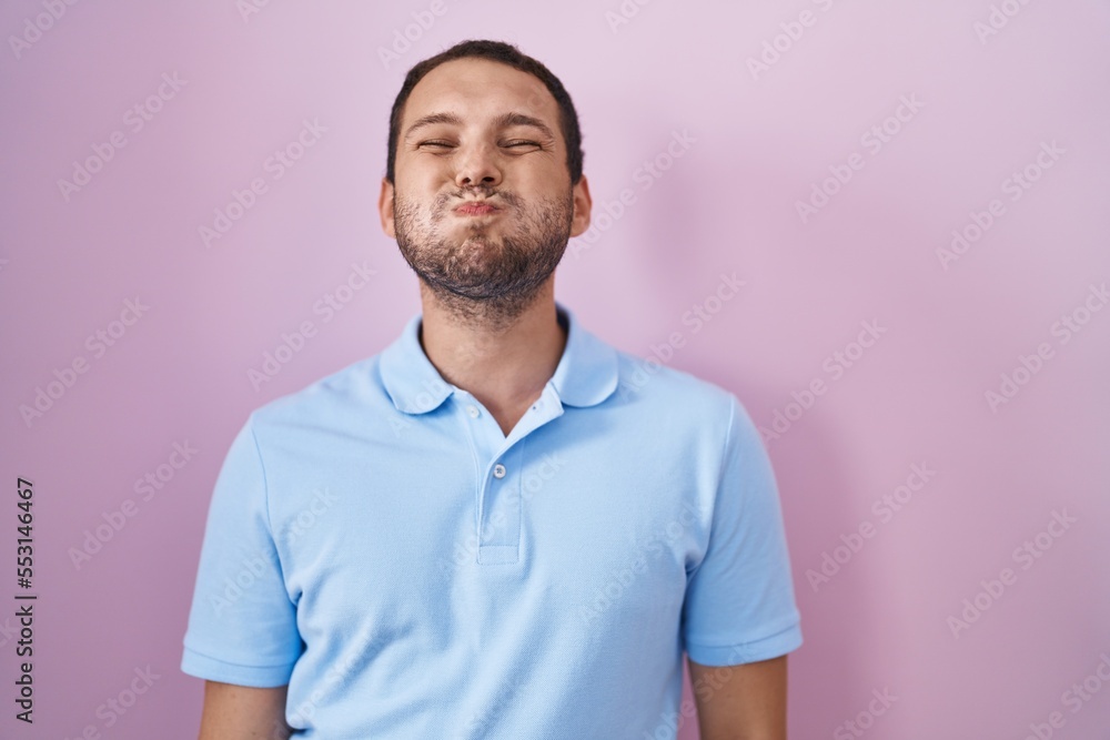 Hispanic man standing over pink background puffing cheeks with funny ...