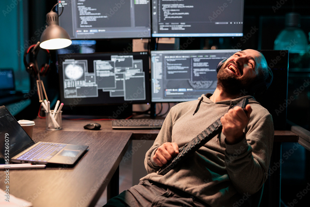 Cheerful programmer singing at air guitar keyboard late at night, working on cloud computing ...