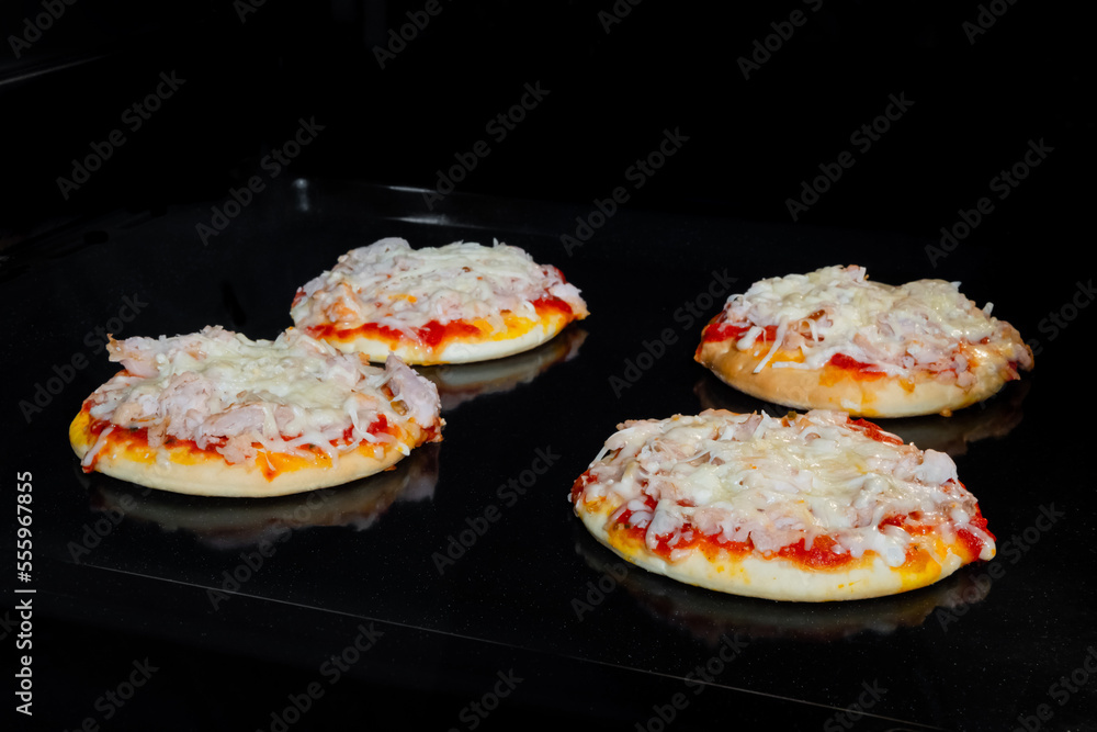Four baked mini pizzas with ham, cheese and sause on tray in electric ...