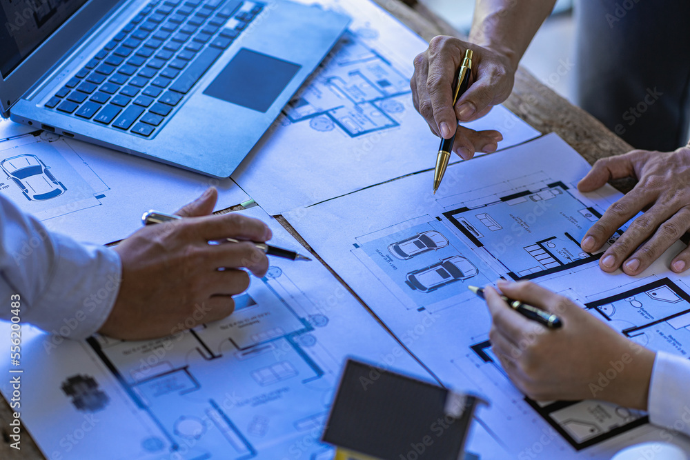 Engineer pointing at blueprint and using laptop to draw building design project in office ...