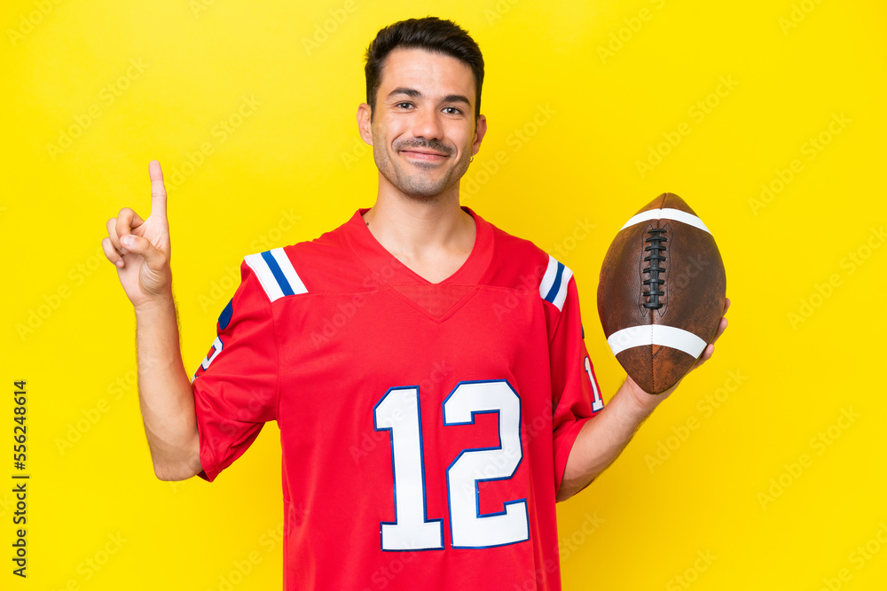 Young handsome man playing rugby over isolated yellow background ...