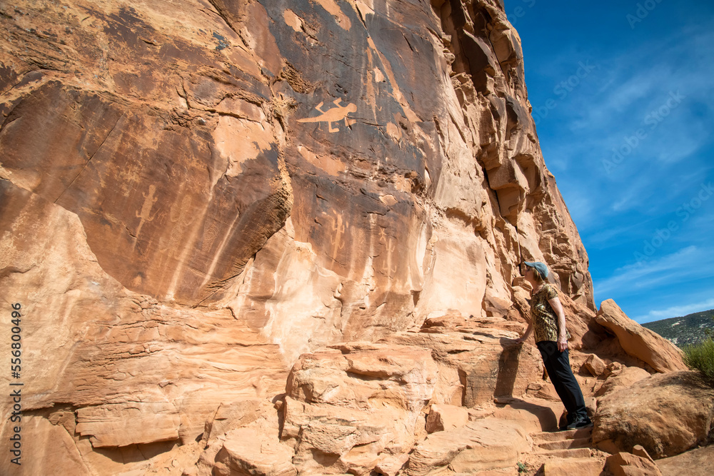 Female tourist admires ancient petroglyphs depicting lizards on a rock ...