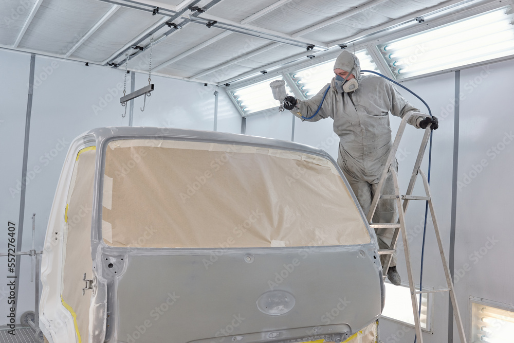 Unrecognisable man wearing work clothes and respirator painting truck ...