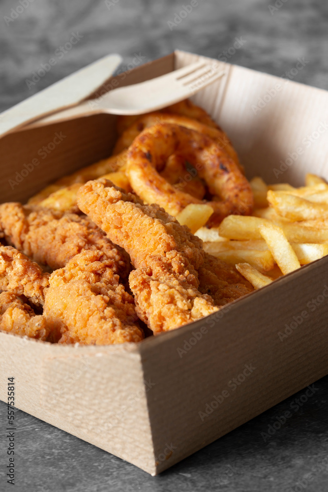 Breaded fried chicken breast with fries and onion rings, in a cardboard ...