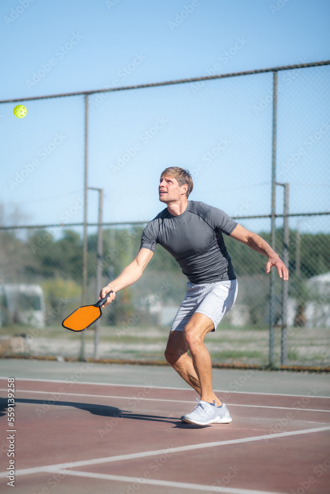 man playing pickleball game, hitting pickleball yellow ball with paddle ...
