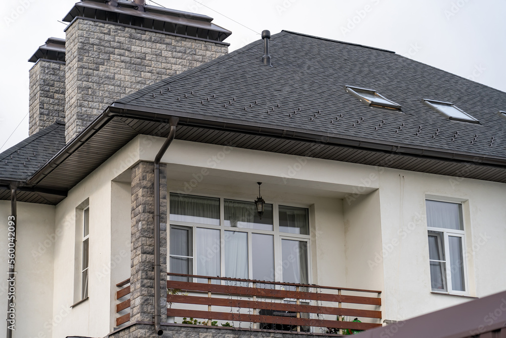 Stucco house with balcony and drainage system on metal roof. Сhimney ...