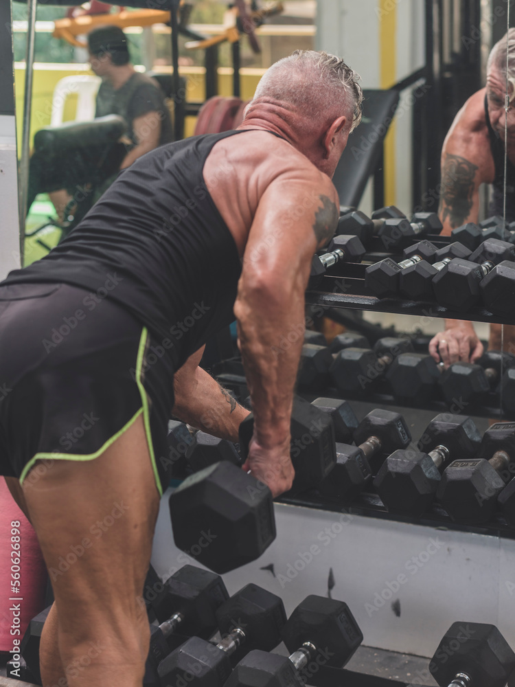 A muscular tanned older German guy does bent over one arm dumbbell rows ...