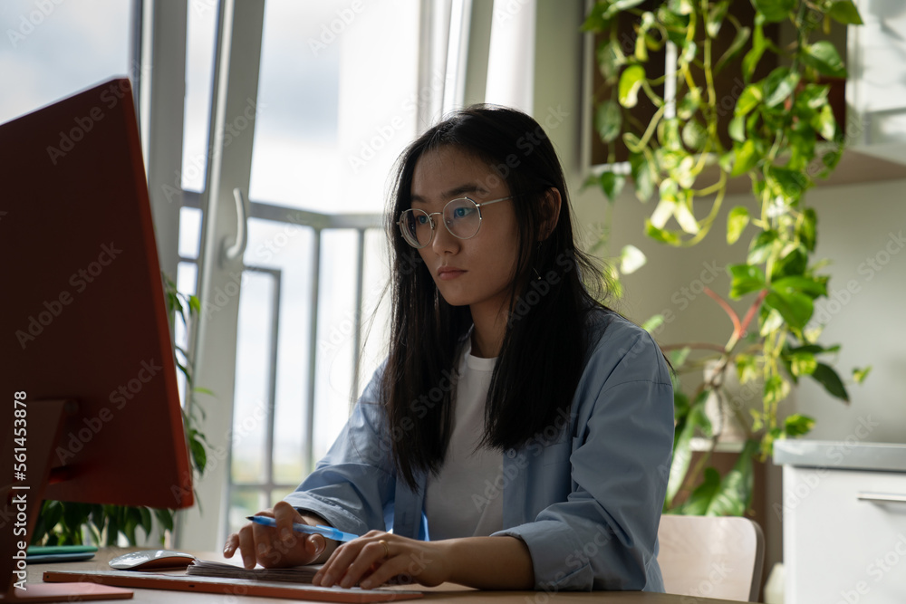 Photo Stock Focused Asian woman IT developer wearing glasses writing code while working remotely ...