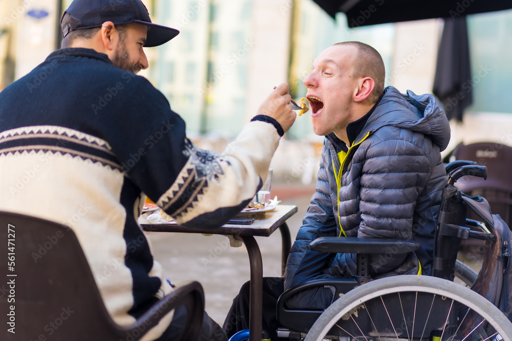 A disabled person eating with the help of a friend having fun, terrace ...
