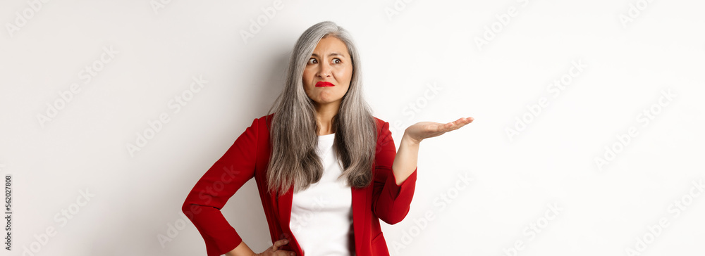 Annoyed and confused asian business woman spread hand sideways and ...