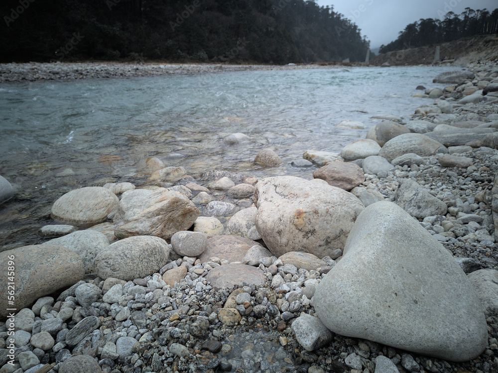 Low angle view of beautiful rocky Teesta river with snowfall and pine ...