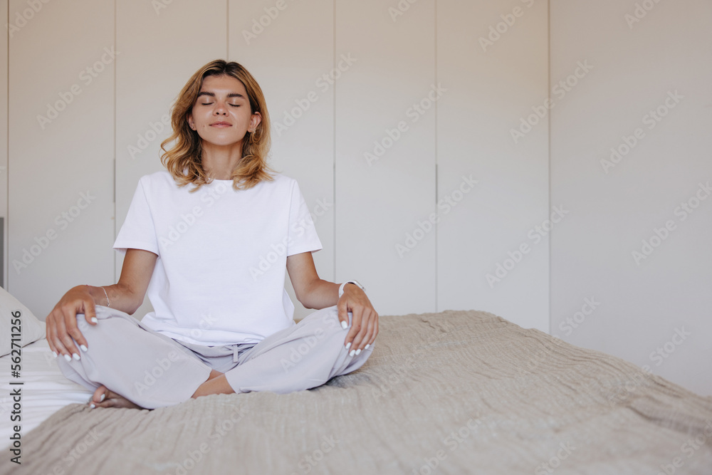 Calm young caucasian girl sitting on bed and meditation in morning at ...