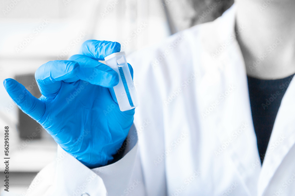 Close up scientist hand holding a spectrophotometry cuvette with blue ...