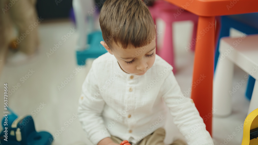 Adorable caucasian boy student sitting on floor with relaxed expression ...