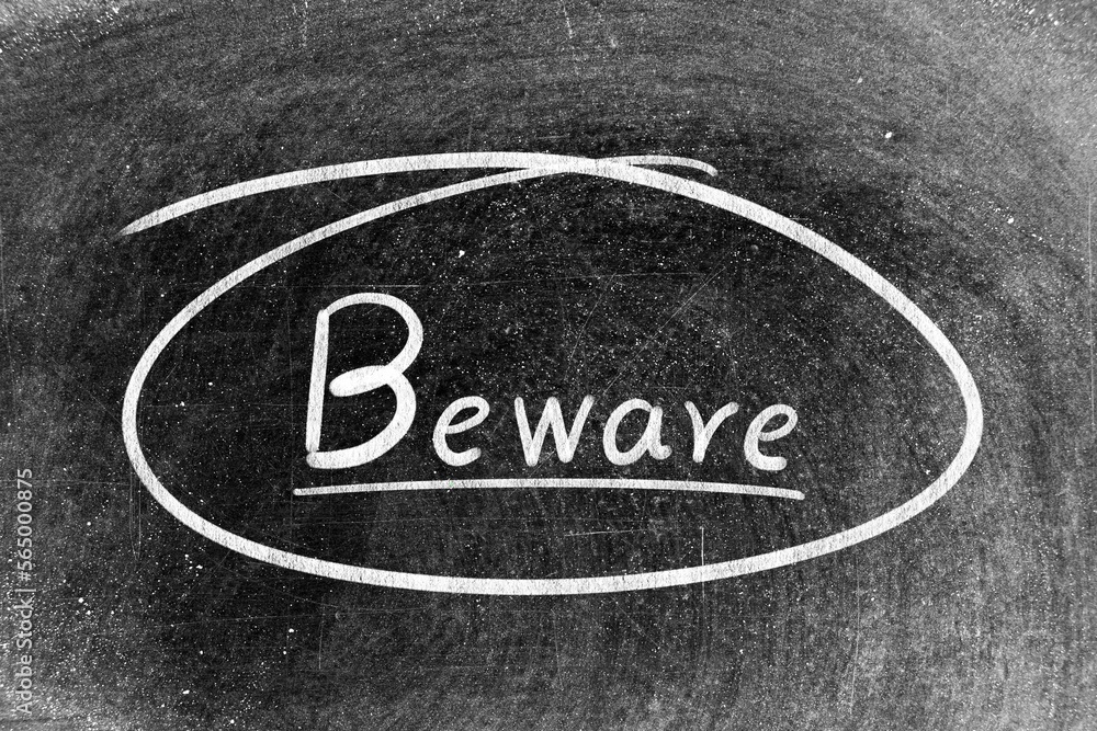 White chalk hand writing in word beware and circle shape on blackboard ...