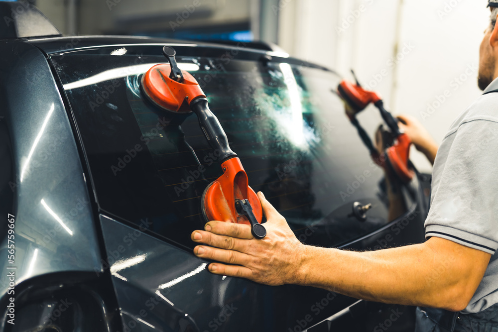 Unrecognisable man instaling rear window pane in the back of car using ...