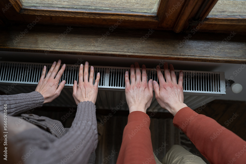 Man and woman warm hands by placing on radiator located by window of ...