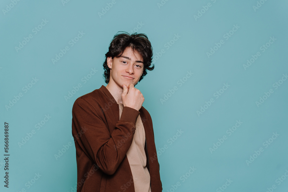 Thoughtful handsome Italian teenager in brown jacket touching chin ...