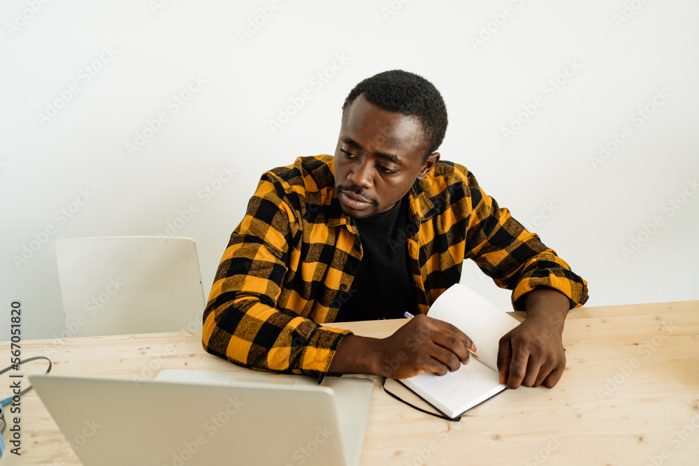 Thoughtful focused black man writing in notepad Stock Photo | Adobe Stock