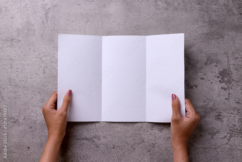 hands holding blank opened tri fold flyer brochure on gray background ...