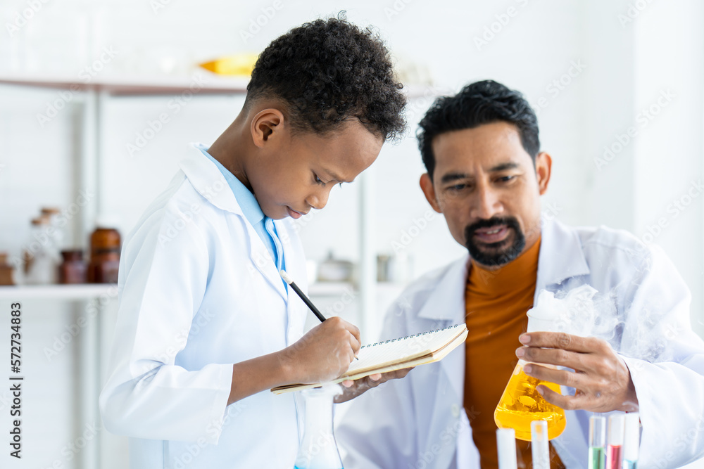 Little african boy in science classroom taking note of the experiment ...