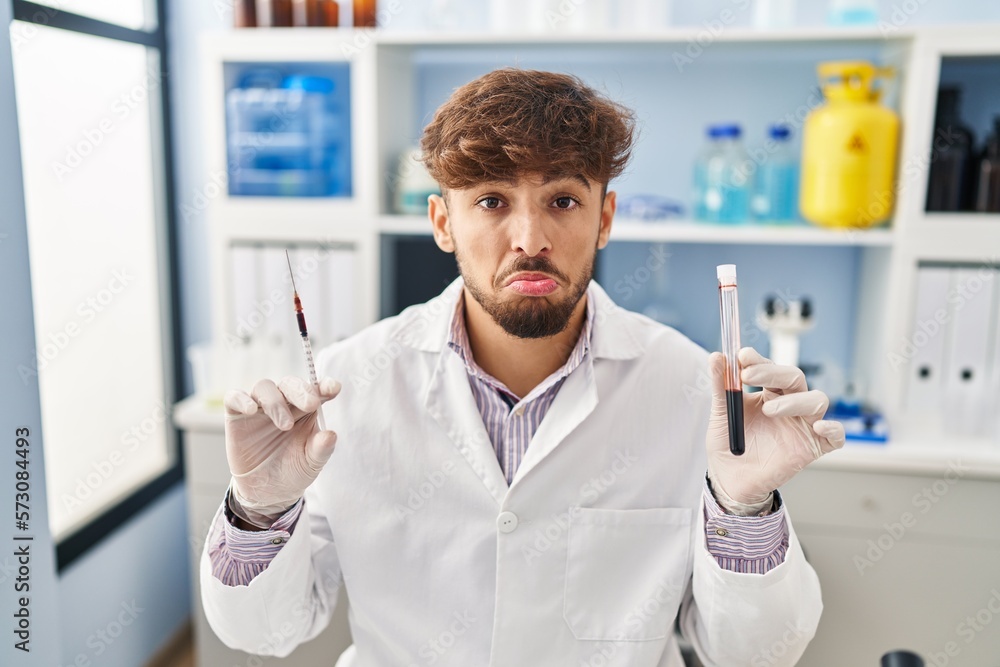 Arab man with beard working at scientist laboratory holding blood sample depressed and worry for ...