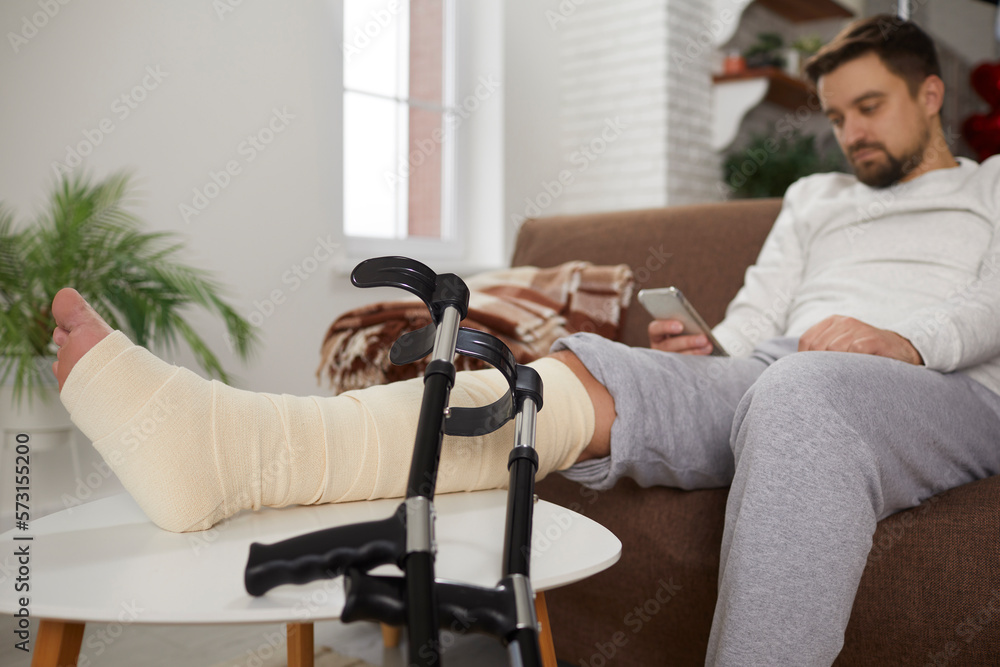 Young man sitting on the sofa at home with his broken injured leg in a ...