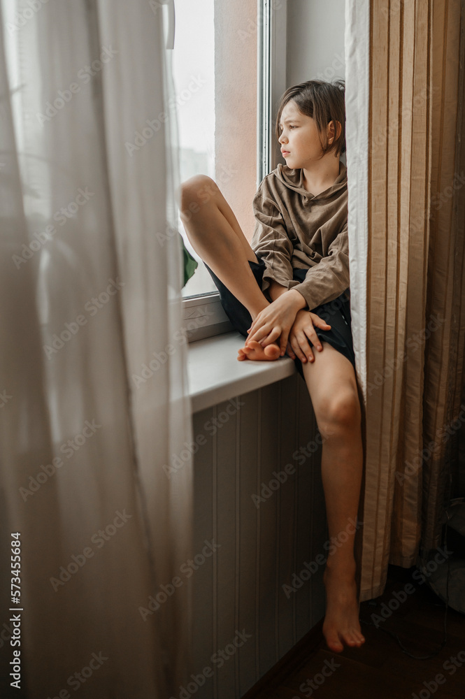 Thoughtful boy sitting on window sill Stock Photo | Adobe Stock