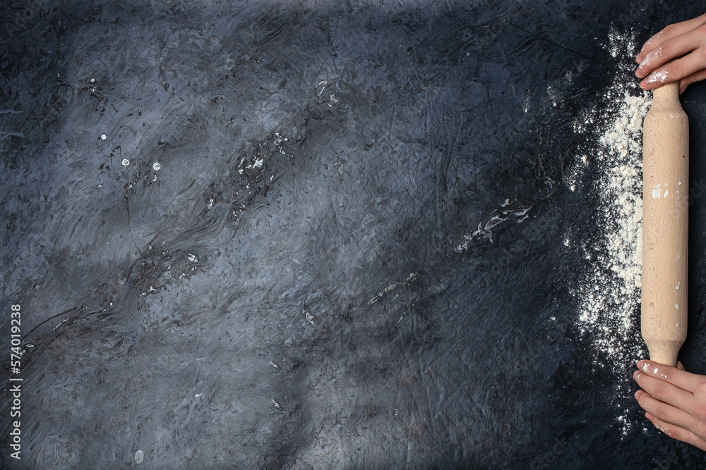 hands keep rolling pin with flour on a dark background. baking ...