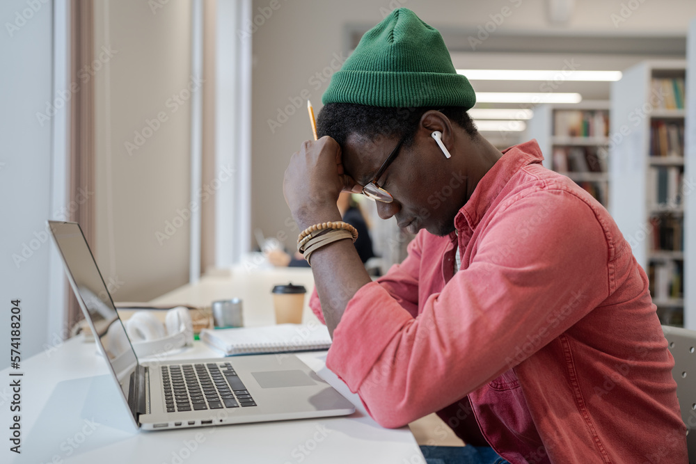 Frustration in distance education. Frustrated young African American guy sitting in front of ...